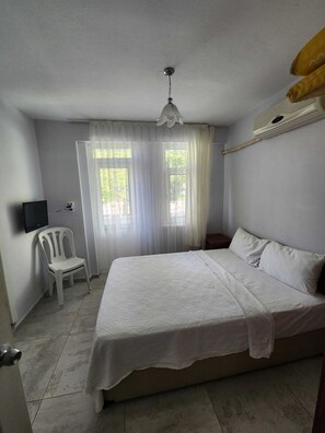 Quarto com cama, cadeira, televisão e janela com cortinas.