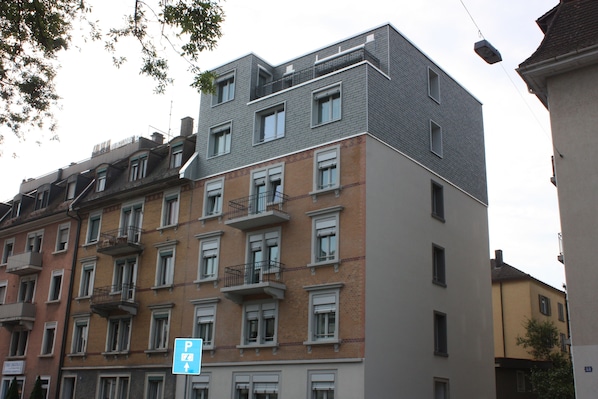 Edifício com vários andares, fachada que combina tijolos e design moderno, com varandas e um aviso de estacionamento visível.