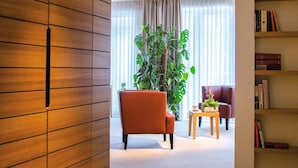 Sala de estar moderna com parede de painéis de madeira, uma planta grande, poltrona vermelha, mesa pequena e estante.