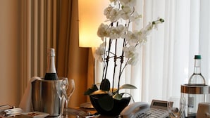 Quarto de hotel com minibar, telefone, um copo de água, garrafa de vinho, arranjo de flores e conjunto de jantar.