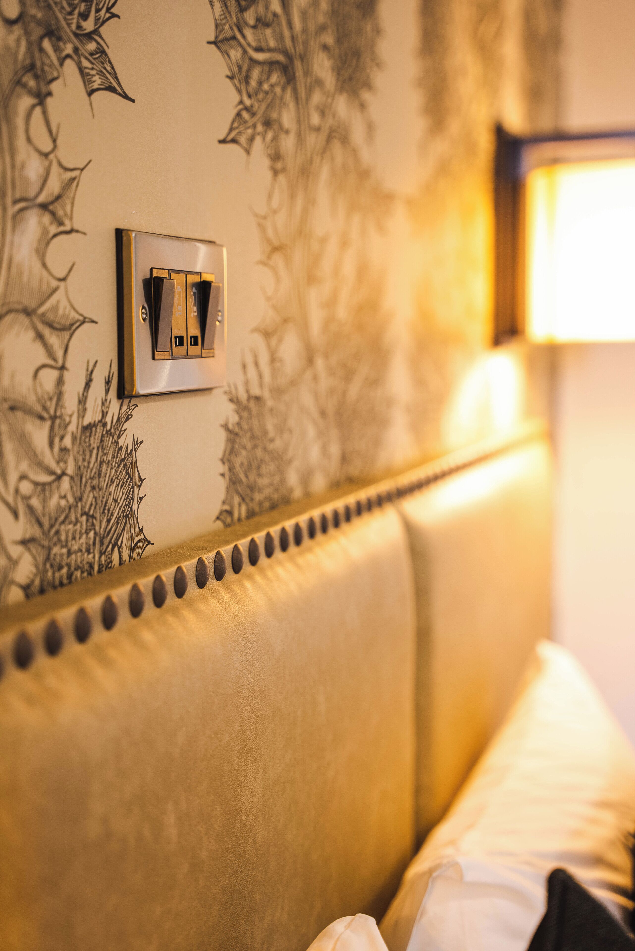Quarto de hotel com cama, interruptor de luz na parede e painel decorativo.