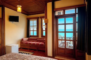 Quarto com um banco de madeira, uma televisão e uma grande janela com vista para o mar.