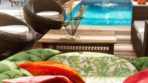 Uma área à beira da piscina com mobiliário de vime, uma pequena mesa com velas e vista para a piscina.