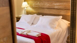 Uma cama bem arrumada com roupa de cama branca e um cobertor vermelho, uma cabeceira de madeira e um objeto decorativo fixado na parede.