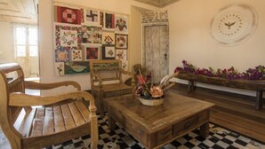 Quarto com chão quadriculado, mobiliário de madeira, parede com exposição de colchas e um relógio.