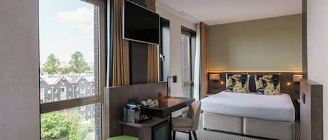 Quarto de hotel com cama, escrivaninha com cadeira, mini-geladeira, televisão e janela grande com cortinas.