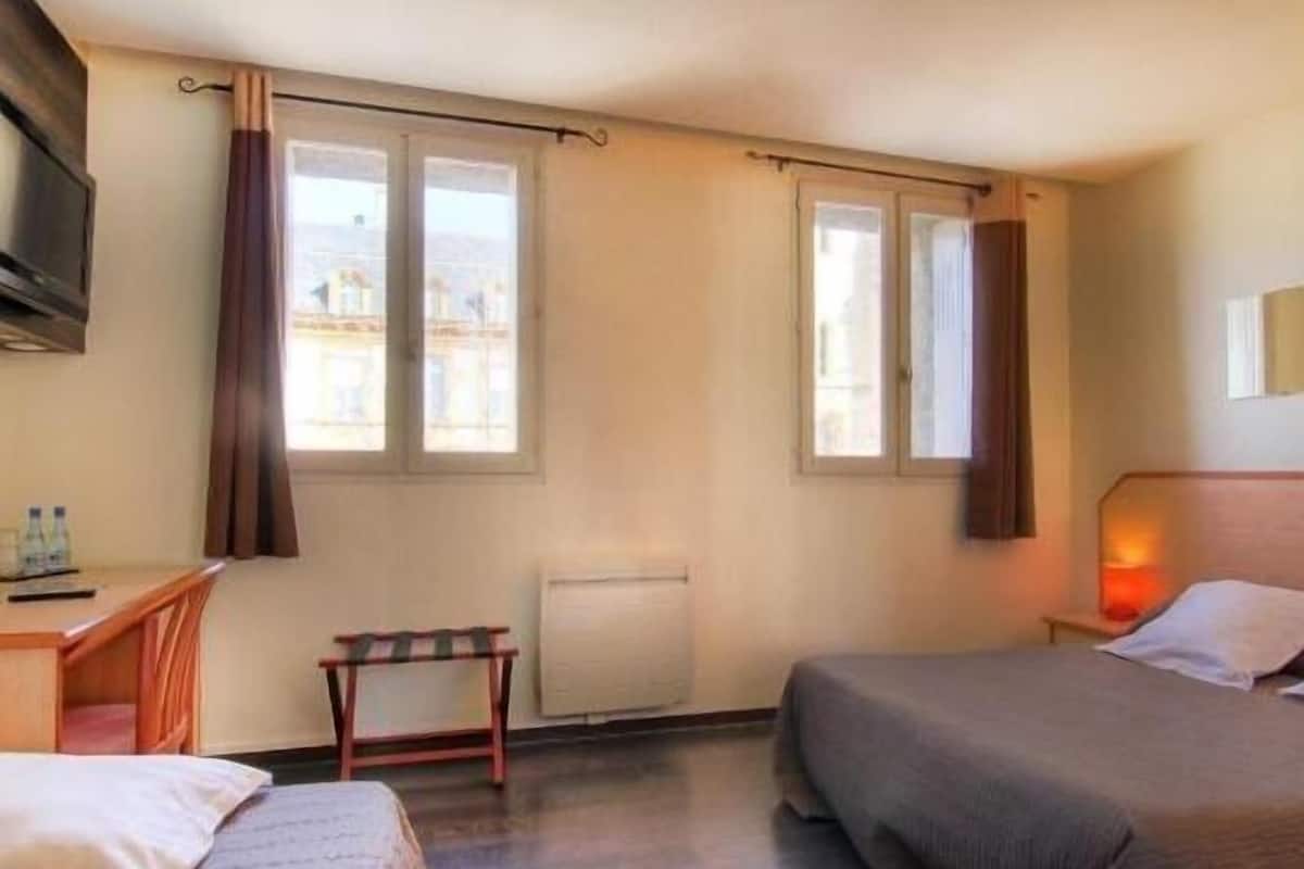 Quarto de hotel com duas camas, uma mesa, uma cadeira e uma janela com cortinas.