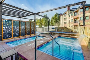 Área de piscina com hidromassagem, deck de madeira e vista para um edifício com varandas.