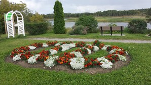 Um parque com um canteiro de flores, um banco e um lago ao fundo.