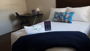 Quarto de hotel com cama, uma placa na cama, uma cadeira, uma mesa e um travesseiro.