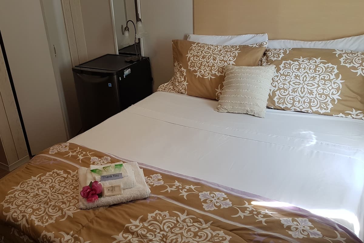 Quarto de hotel com cama bem arrumada, mesa de cabeceira, uma cadeira e um guarda-roupa.
