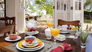 Mesa posta para dois, com tigela de frutas, jarra, copo de suco de laranja e xícara de café.