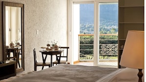 Quarto com uma grande janela, varanda com vista para o campo, mesa de jantar com jogo de chá e espelho na parede.