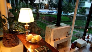 Uma sala de estar moderna com lareira, uma mesa de jantar com uma cesta de frutas e vista para uma piscina e jardim.