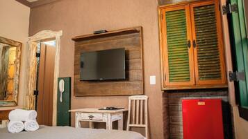 Quarto com cama, televisão na parede, mesinha, cadeira, guarda-roupa e frigorífico vermelho.