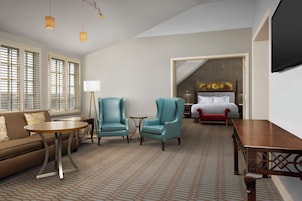 Quarto de hotel com sofá, duas poltronas, uma mesinha, cama e televisão.