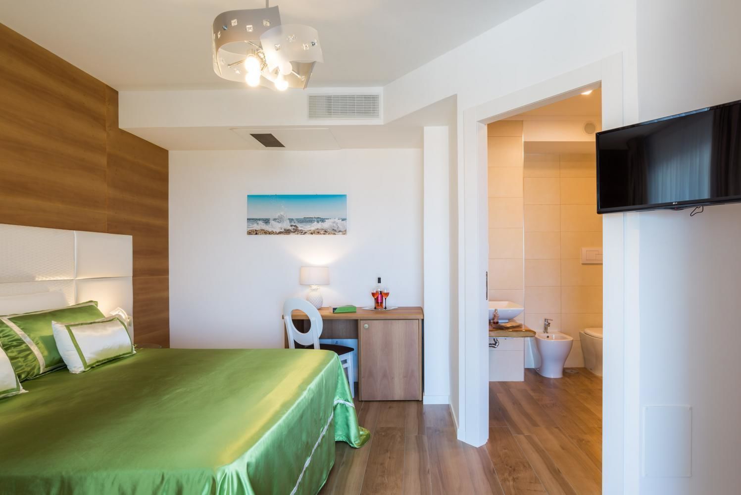 Quarto de hotel com cama, escrivaninha, cadeira e banheiro com vaso sanitário e pia.