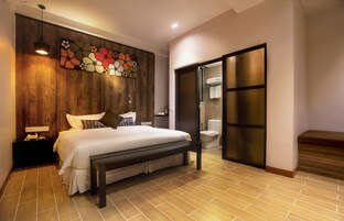 Quarto com cabeceira de madeira, uma cama grande com roupa de cama branca, mesa de cabeceira com abajur e um banco.