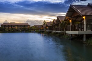 Um hotel na orla com vários edifícios, um rio calmo e um céu ao pôr do sol.