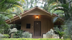 Uma cabana de madeira com telhado inclinado, rodeada por vegetação exuberante.