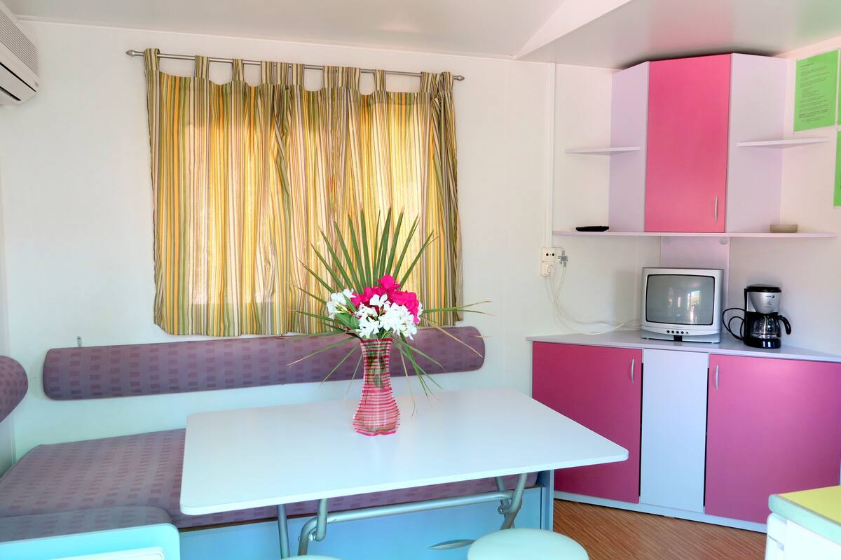 Uma cozinha compacta com televisão, cafeteira e armários cor-de-rosa.