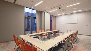 Uma sala de conferências com uma mesa comprida, cadeiras, uma tela de projetor e grandes janelas.