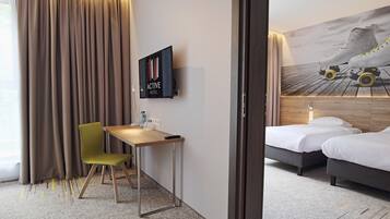 Quarto de hotel com escrivaninha, cadeira, duas camas, televisão e um mural com patins.