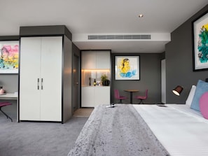 Quarto moderno com cama, escrivaninha, guarda-roupa e um pequeno espaço de refeições.