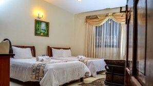 Quarto de hotel com duas camas, uma escrivaninha, uma cadeira, um quadro e uma janela com cortinas.