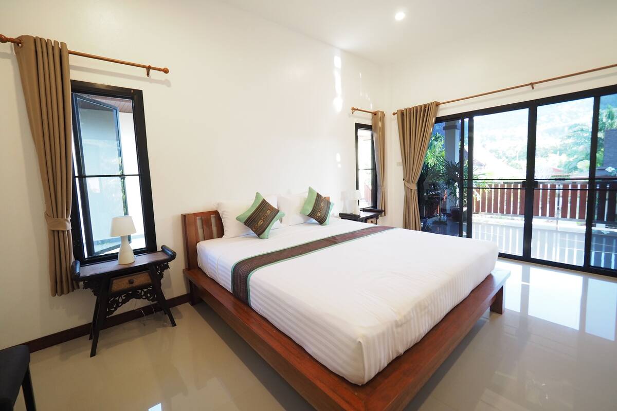 Um quarto espaçoso com uma cama grande, uma mesa de cabeceira com abajur e vista para uma varanda.