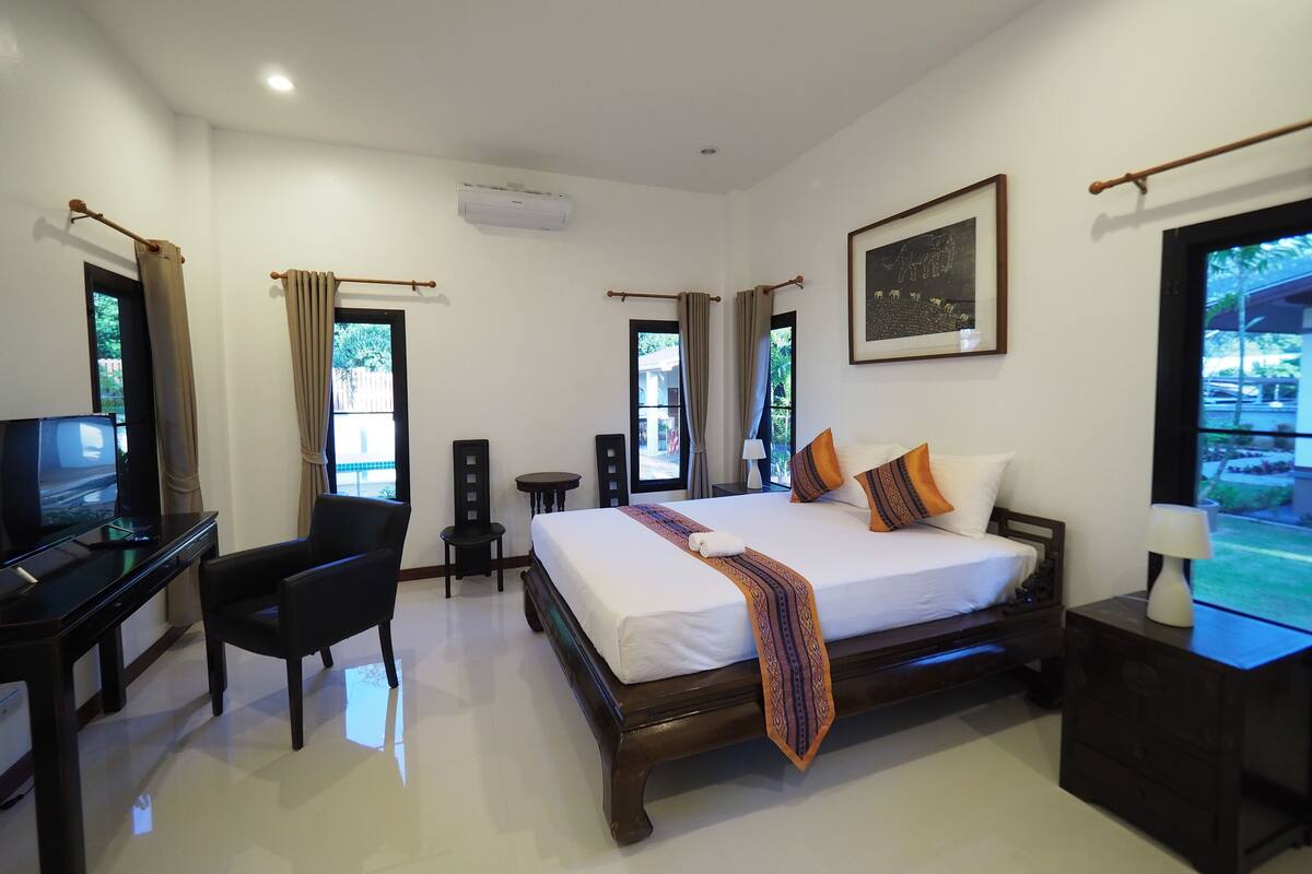 Quarto de hotel com cama, escrivaninha, cadeira, televisão e janela com cortinas.