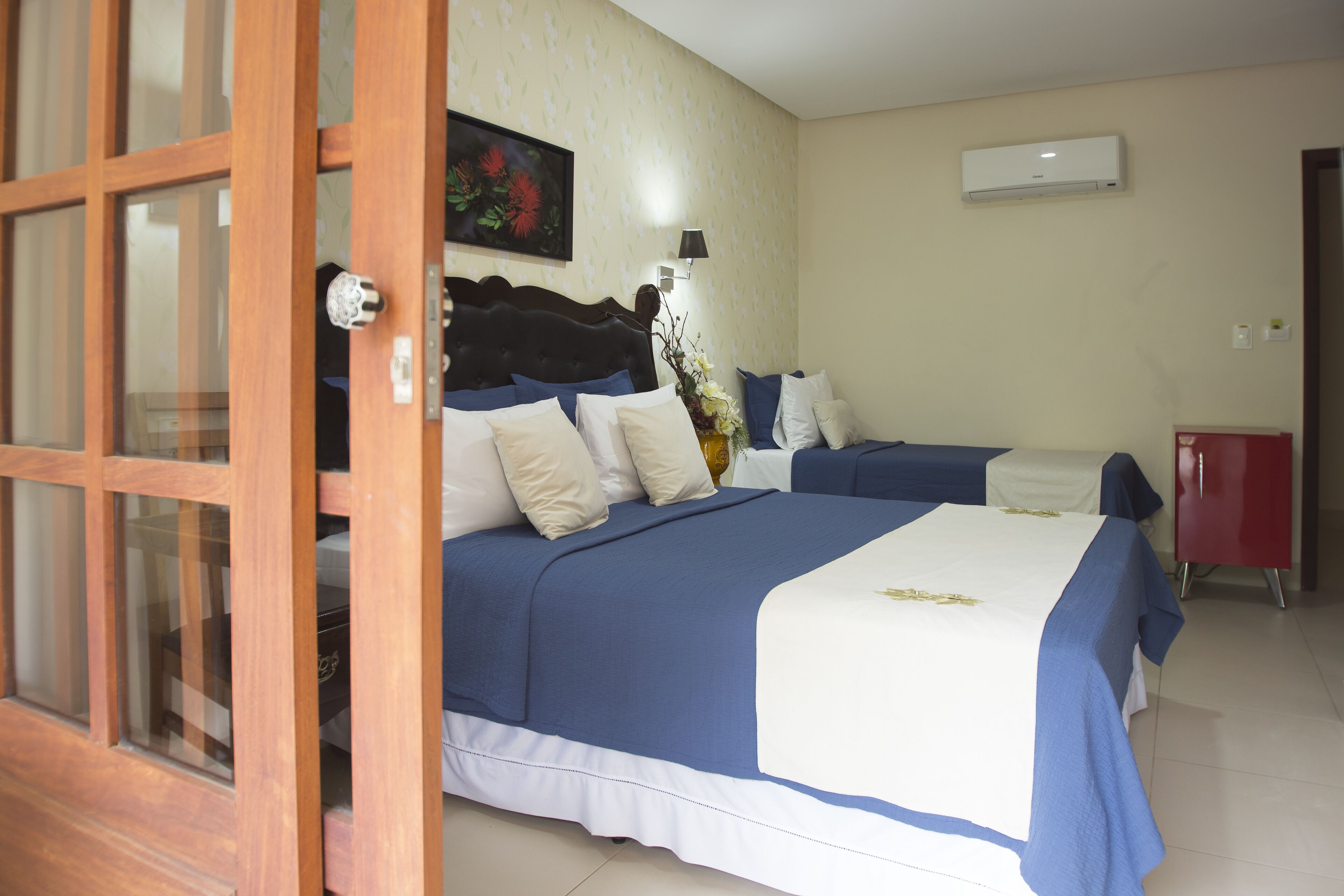 Quarto de hotel com uma cama grande, uma escrivaninha, um guarda-roupa e um aparelho de ar condicionado na parede.
