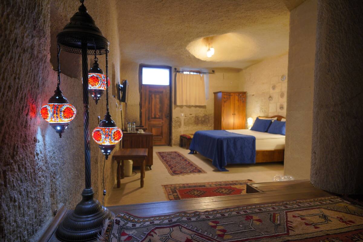Um quarto com uma cama, mesa de cabeceira, penteadeira de madeira e uma janela com cortinas.