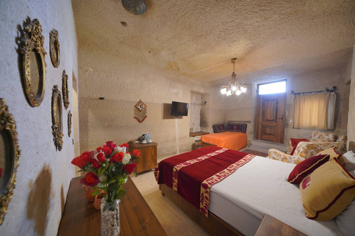 Quarto com uma cama grande, cômoda de madeira, televisão e janela com cortinas.