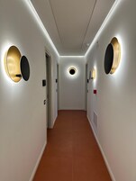 Um corredor com arandelas modernas e uma luminária central no teto.