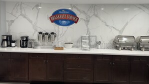 Balcão de café da manhã com máquinas de café, uma torradeira e uma placa com a inscrição 'Breakfast Corner'.