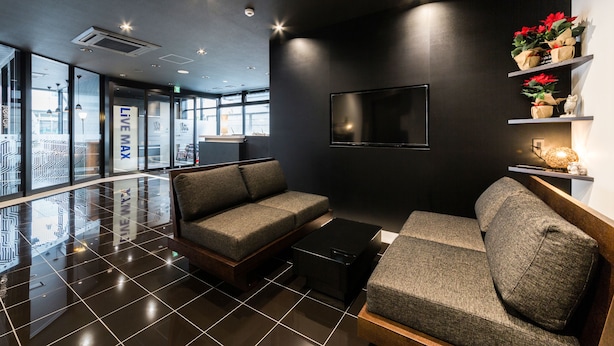 Um lobby moderno com esquema de cores preto e branco, área de estar com sofás cinzas, TV de tela plana na parede e balcão de recepção.
