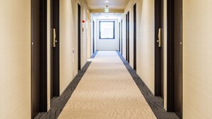 Corredor de hotel com piso coberto por carpete, portas em ambos os lados e uma janela no final.