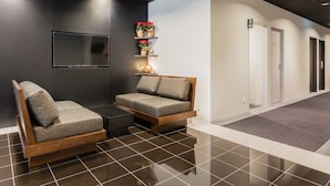 Uma área de espera moderna com dois sofás, uma televisão de tela plana e uma estante com objetos decorativos.