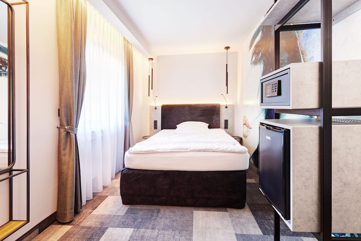 Quarto de hotel com cama, cortinas, televisão na parede e frigorífico.