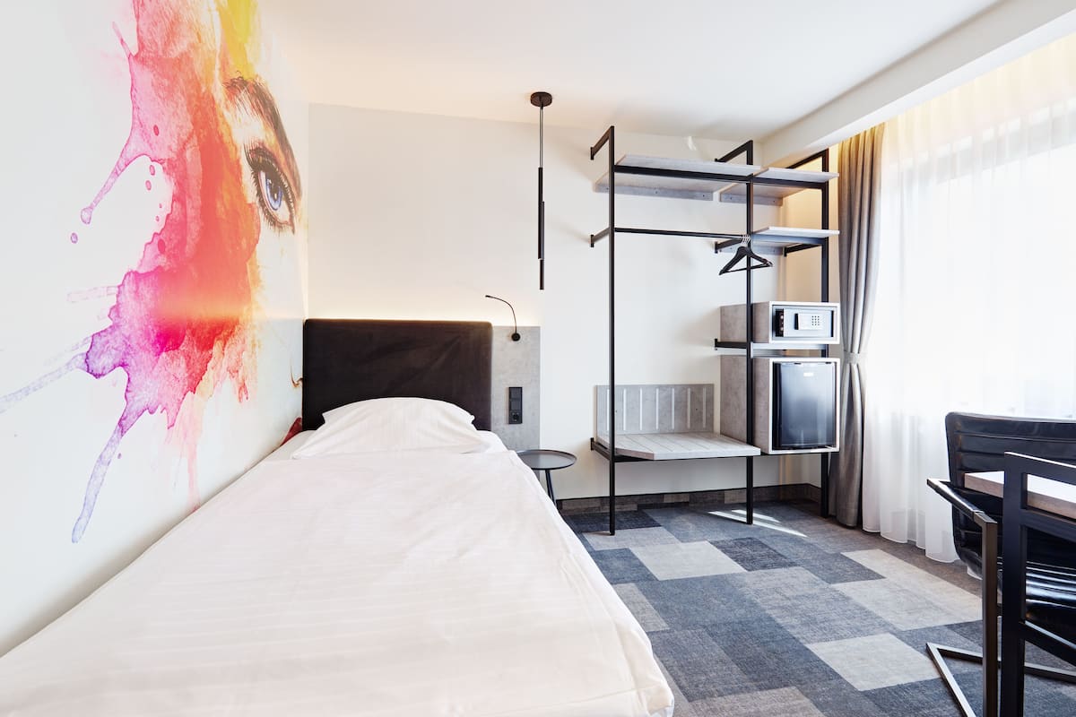 Quarto de hotel com cama, escrivaninha, cadeira, televisão e estante.