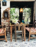 Uma mesa de madeira rústica com cadeiras, um vaso de flores e vista para o verde através de uma janela.