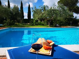Vista da piscina com uma mesa posta para refeição, incluindo pão, tomates e um copo de vinho tinto.