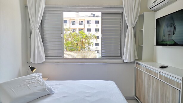 Quarto com cama, televisão e janela com cortinas.