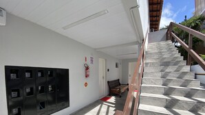 Escada que leva a um segundo andar, extintor de incêndio e um banco em um corredor com piso de azulejos.