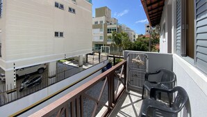 Varanda com grade de metal, cadeira suspensa e vista para edifícios vizinhos e veículos estacionados.
