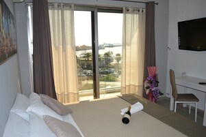 Quarto de hotel com cama, escrivaninha, cadeira, televisão e vista para um porto de iates.