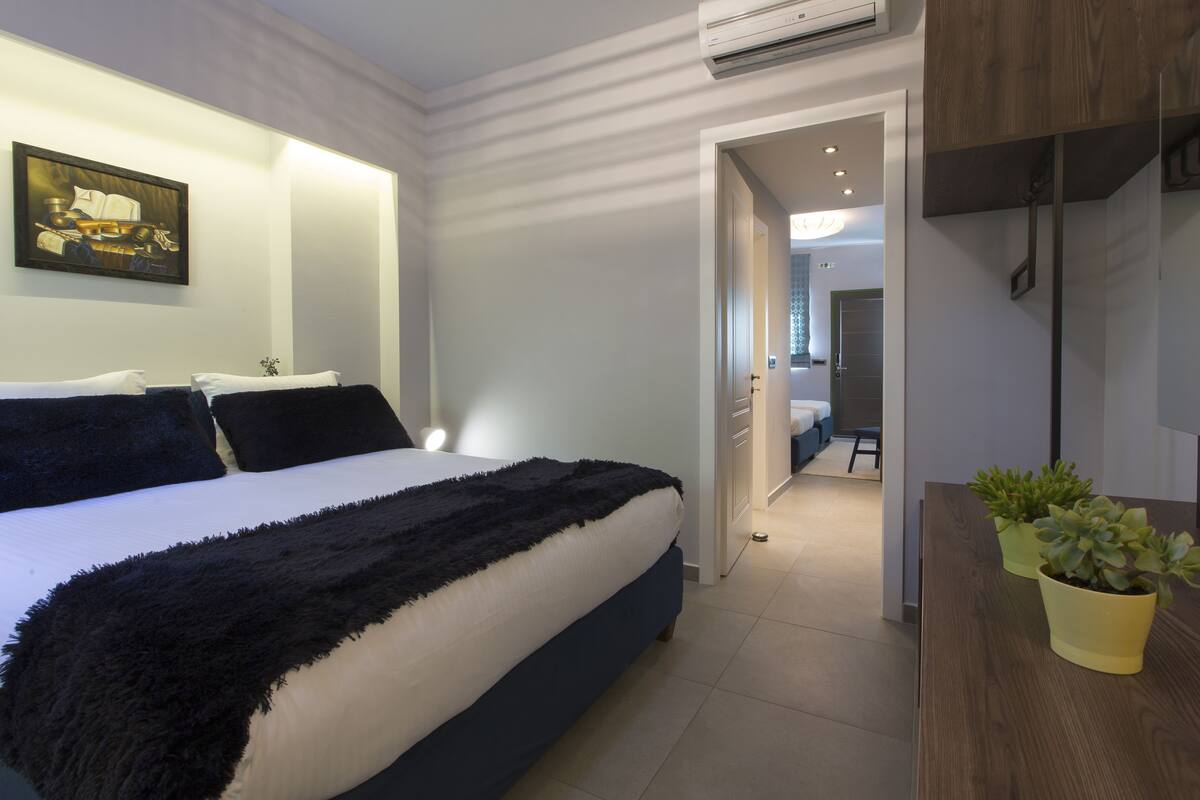 Quarto de hotel moderno com uma cama grande, um quadro na parede e um vaso de planta sobre uma mesa de madeira.