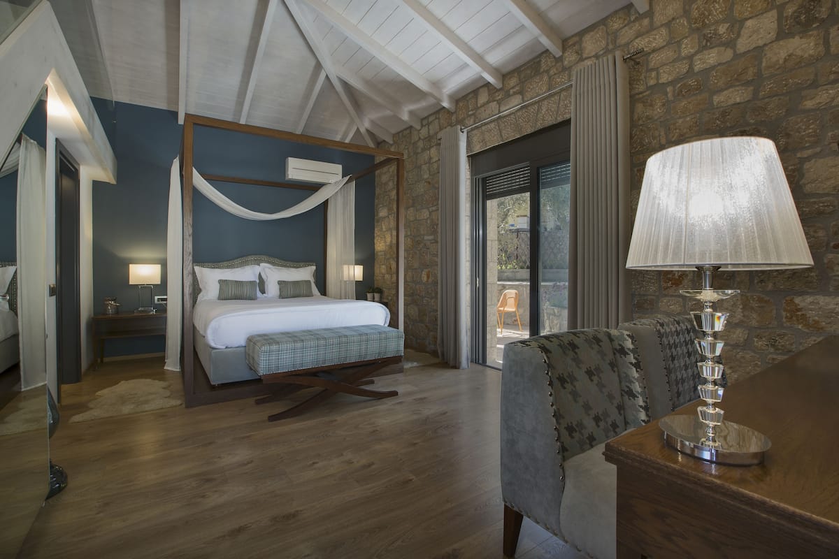 Quarto com cama, mesa de cabeceira, abajur e vista para o exterior.
