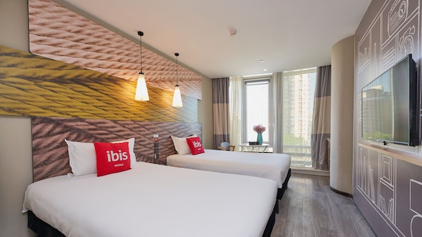 Quarto de hotel com duas camas, uma televisão e uma janela grande com cortinas.